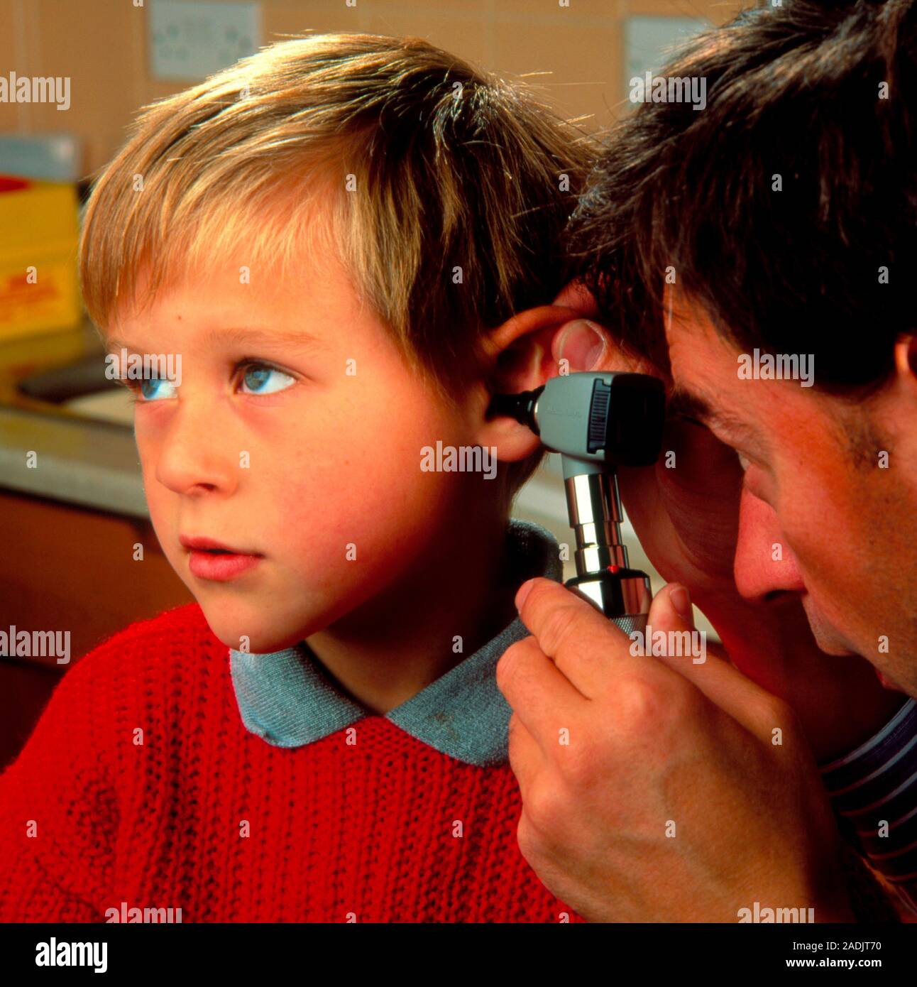 Ear examination. A doctor examines a child's ear for excessive wax and ...