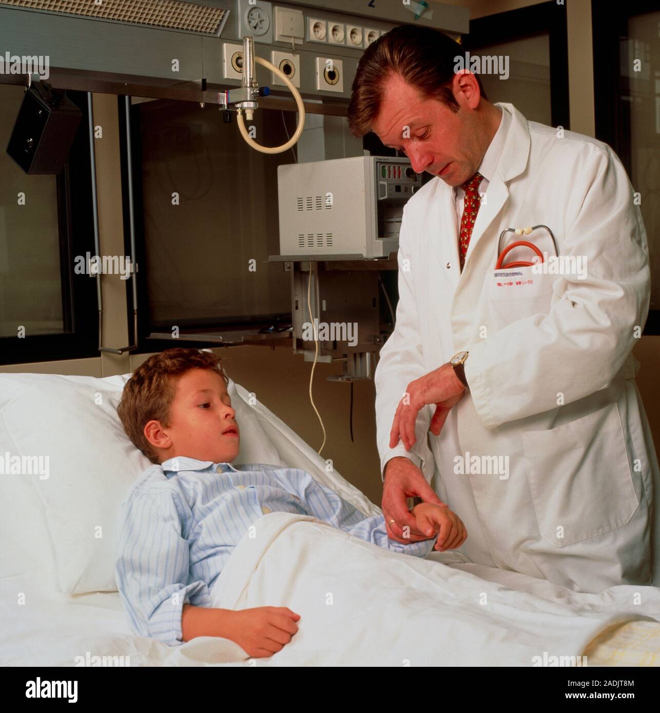 Pulse measurement. Doctor takes the pulse rate of a young boy in bed in ...