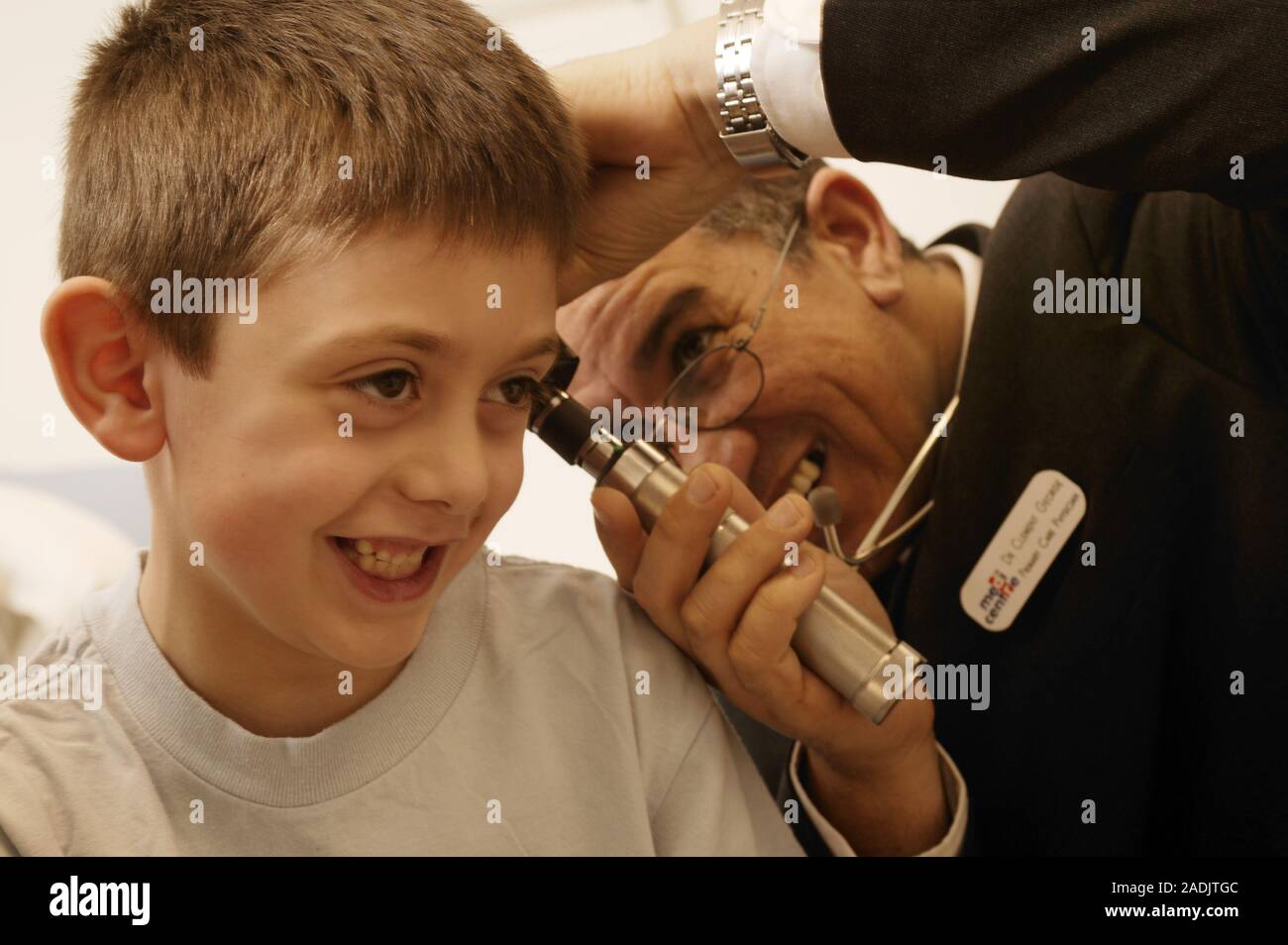 Ear examination. General practice (GP) doctor examining a boy's ear. He ...