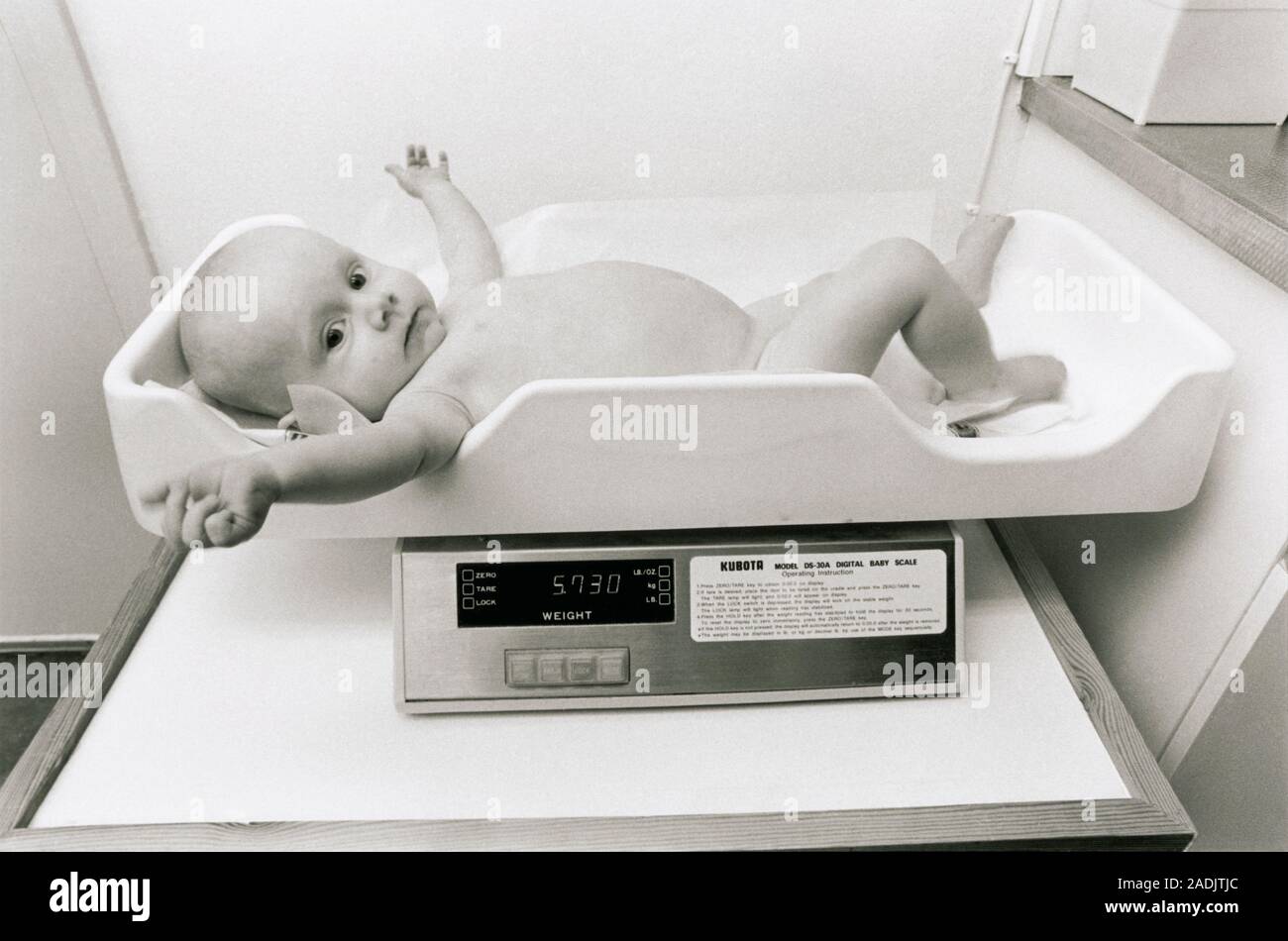 MODEL RELEASED. Paediatric check-up. Baby being weighed during a ...