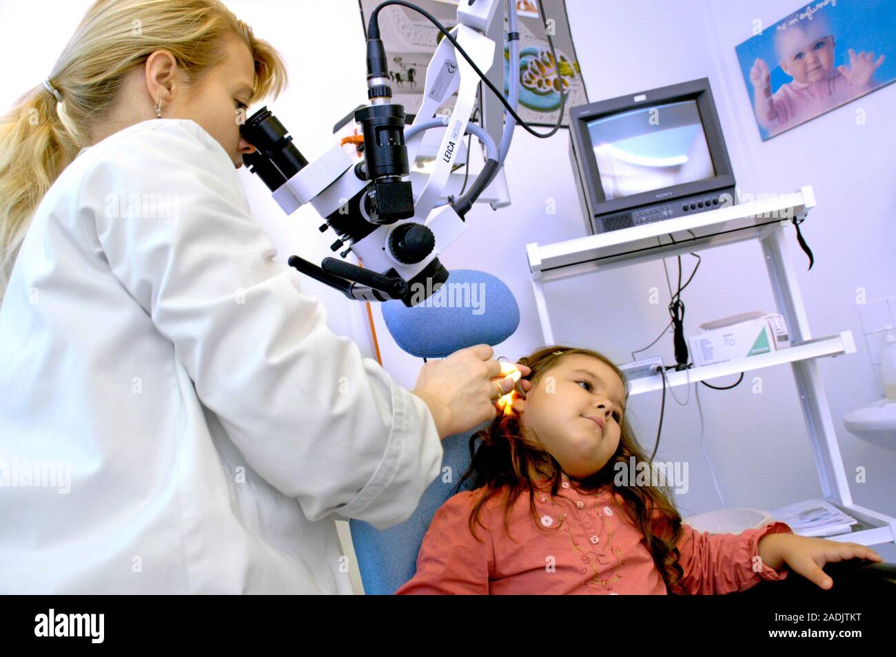 Ear examination. Doctor using a ceiling-mounted microscope to examine a ...