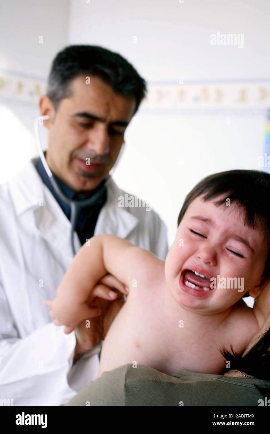 Paediatric examination. Baby boy crying as a doctor uses a stethoscope ...