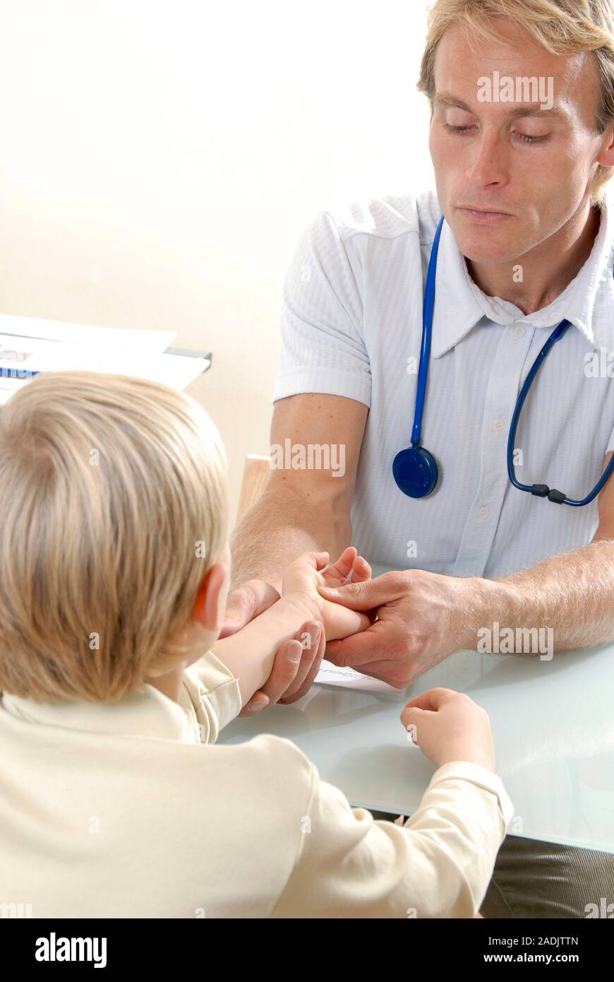 Paediatric examination. Paediatrician examining a young boy's hand ...