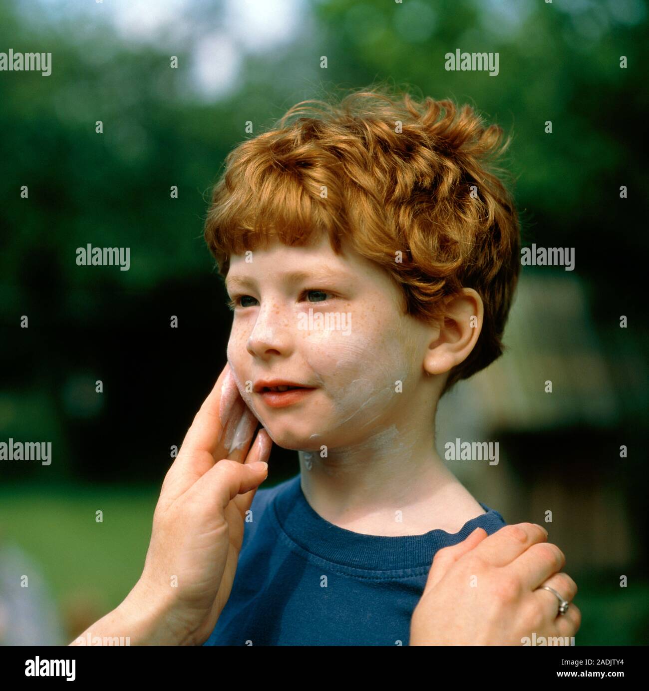 Suncream. Hands of mother apply sunblock cream to the face of her red ...