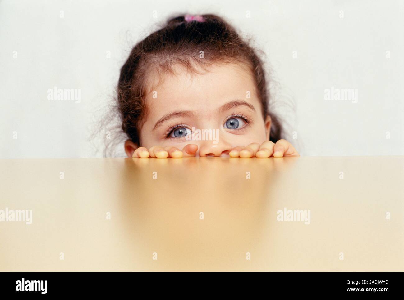 MODEL RELEASED. Young girl hiding. Six year old girl peering over a ...