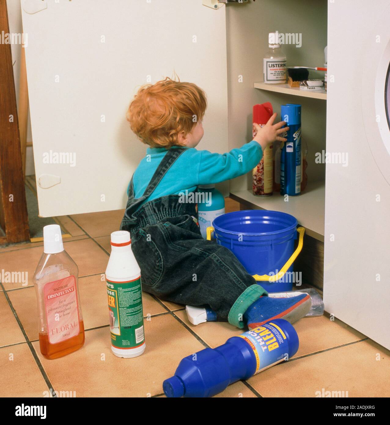 Child safety. Eighteen month old boy playing with bottles of bleach and ...