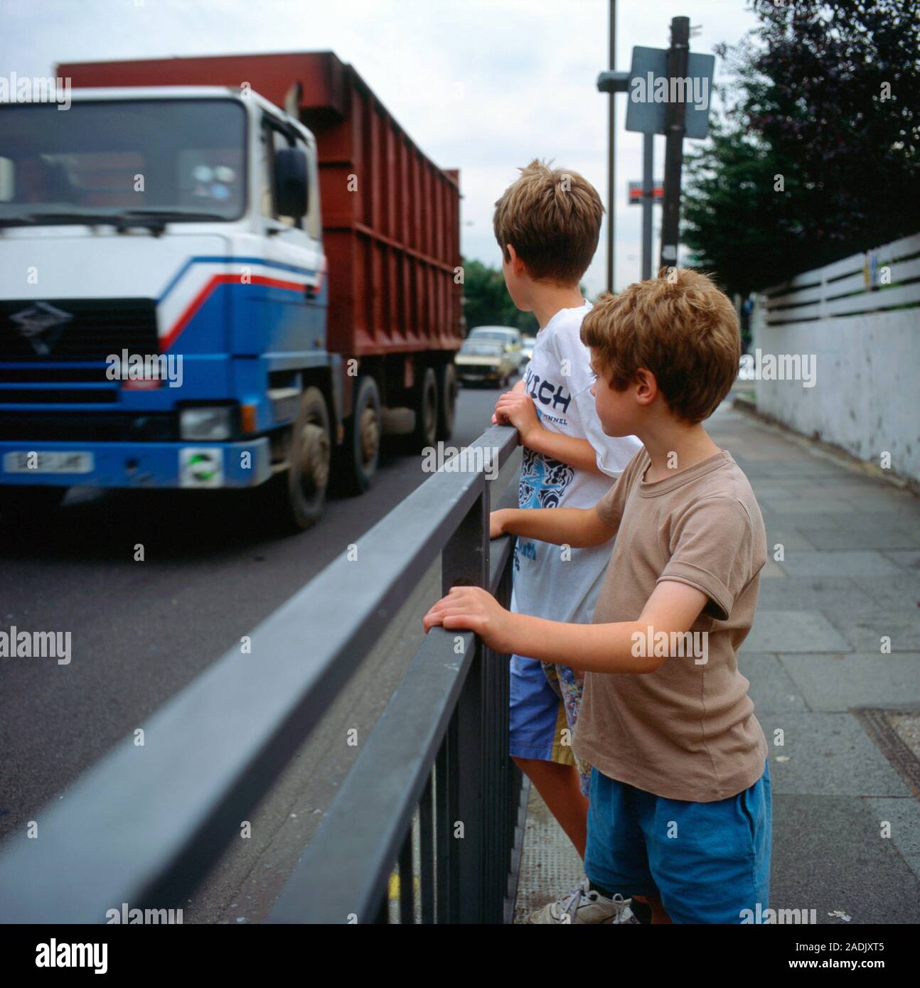 Traffic danger. Two boys standing next to a busy road. The barrier is ...