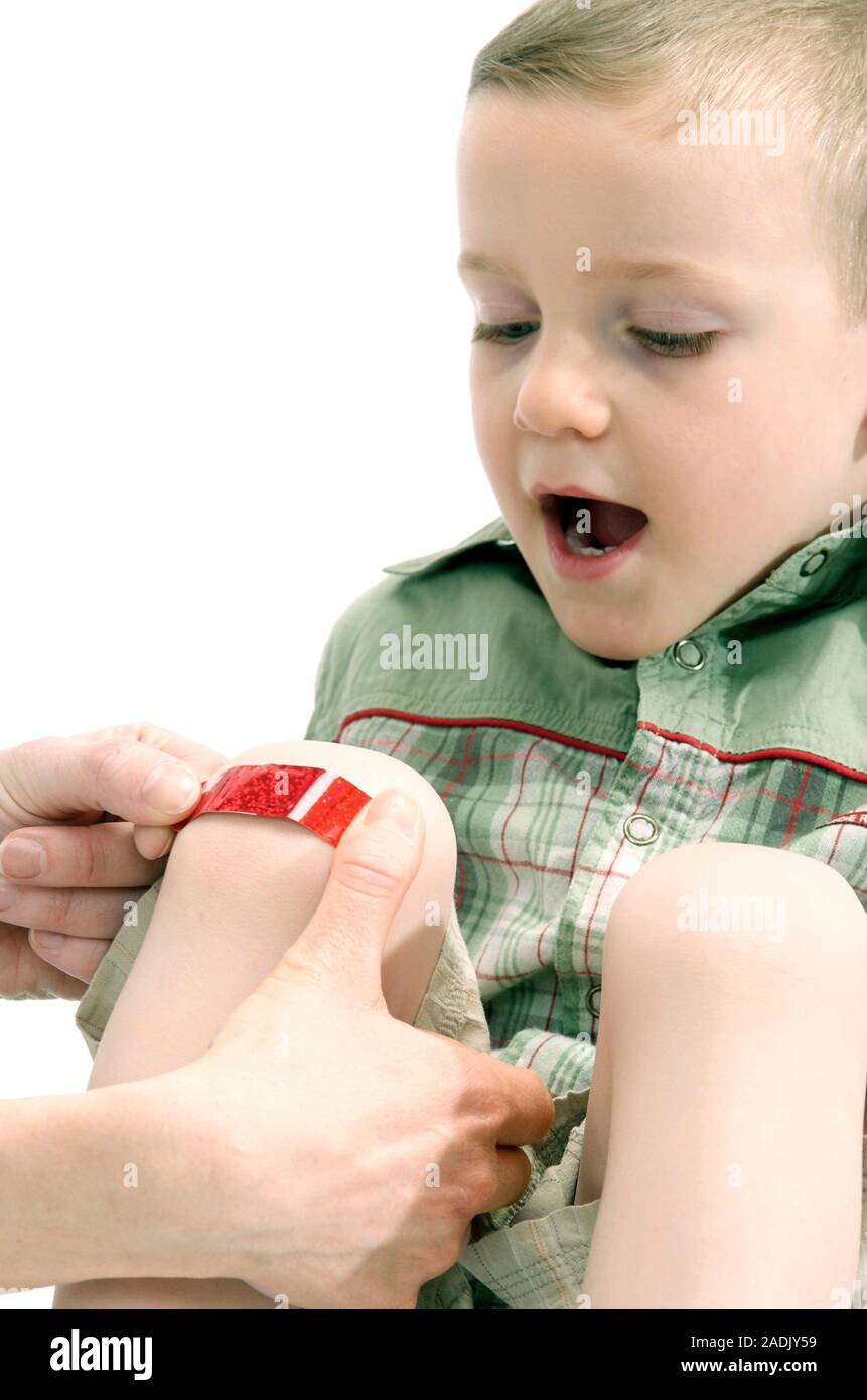 Injured boy. Mother applying a plaster to her son's sore knee. The ...