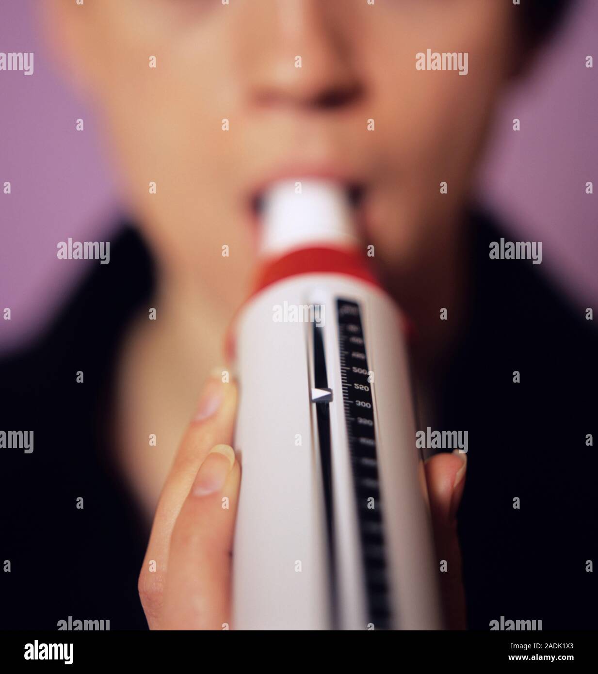 Lung function test. Woman breathing into a peak flow meter (spirometer ...