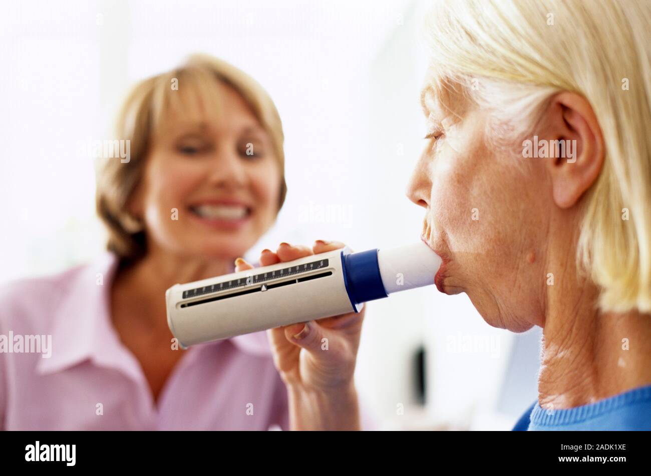 Lung function test. 63-year-old woman breathing into a peak flow meter ...