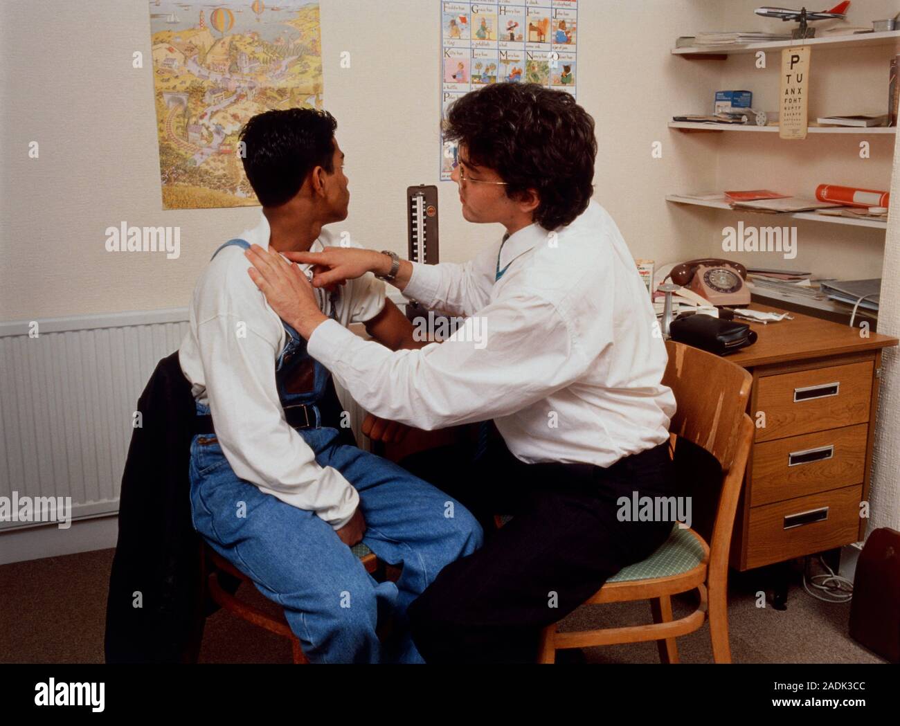 Neck examination. General practice doctor examining the neck of a male ...