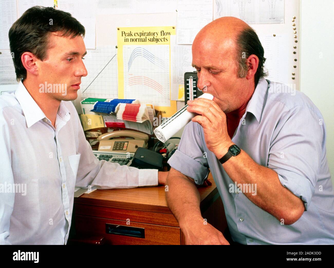 Middle-aged man blowing into a peak flow meter during a visit to his ...