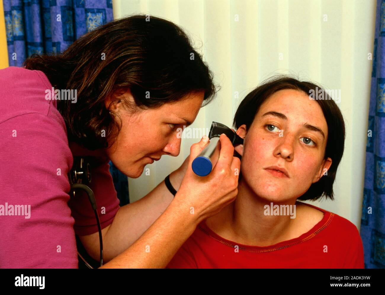 Ear examination. General practice (GP) doctor using an otoscope to ...