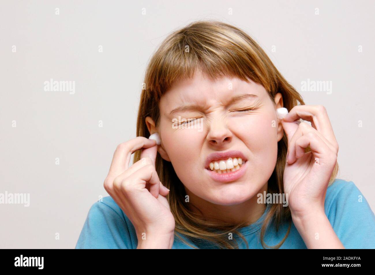 MODEL RELEASED. Noise pollution. 18-year-old woman putting ear plugs in ...
