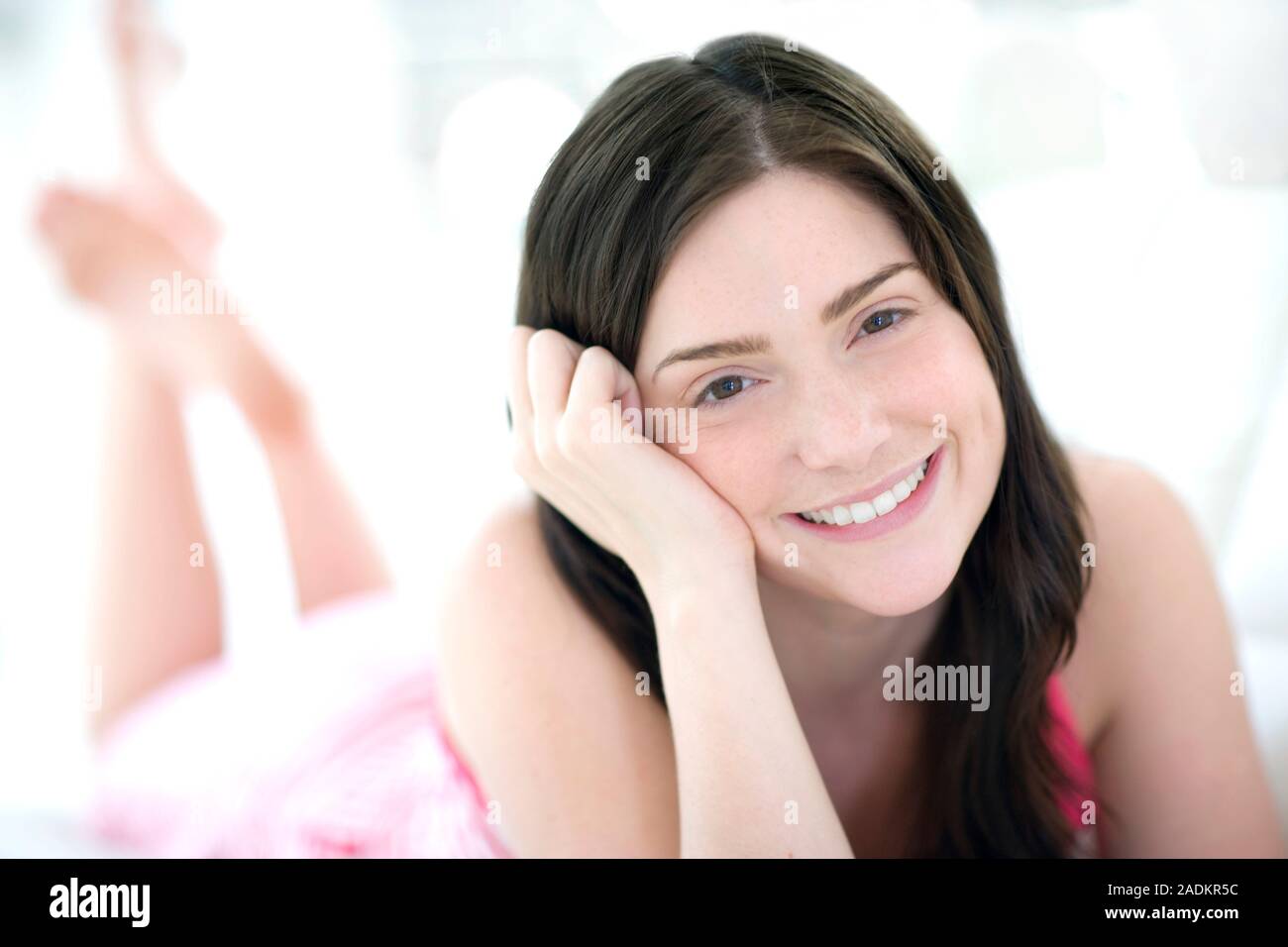 MODEL RELEASED. Happy woman lying down and resting her head on her hand. She is in her twenties ...