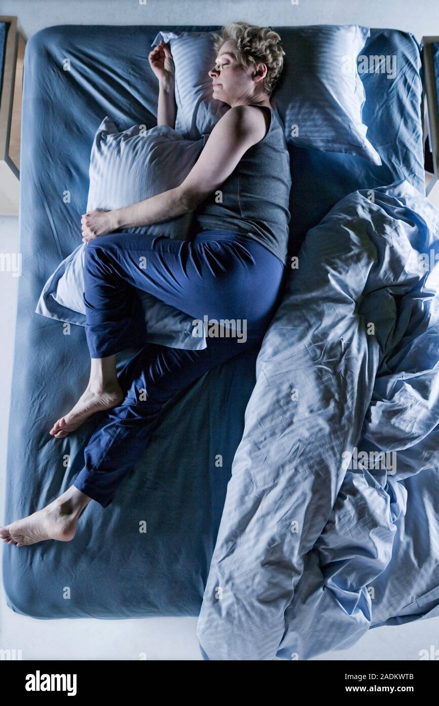 MODEL RELEASED. Woman sleeping in a bed with the covers pulled away ...