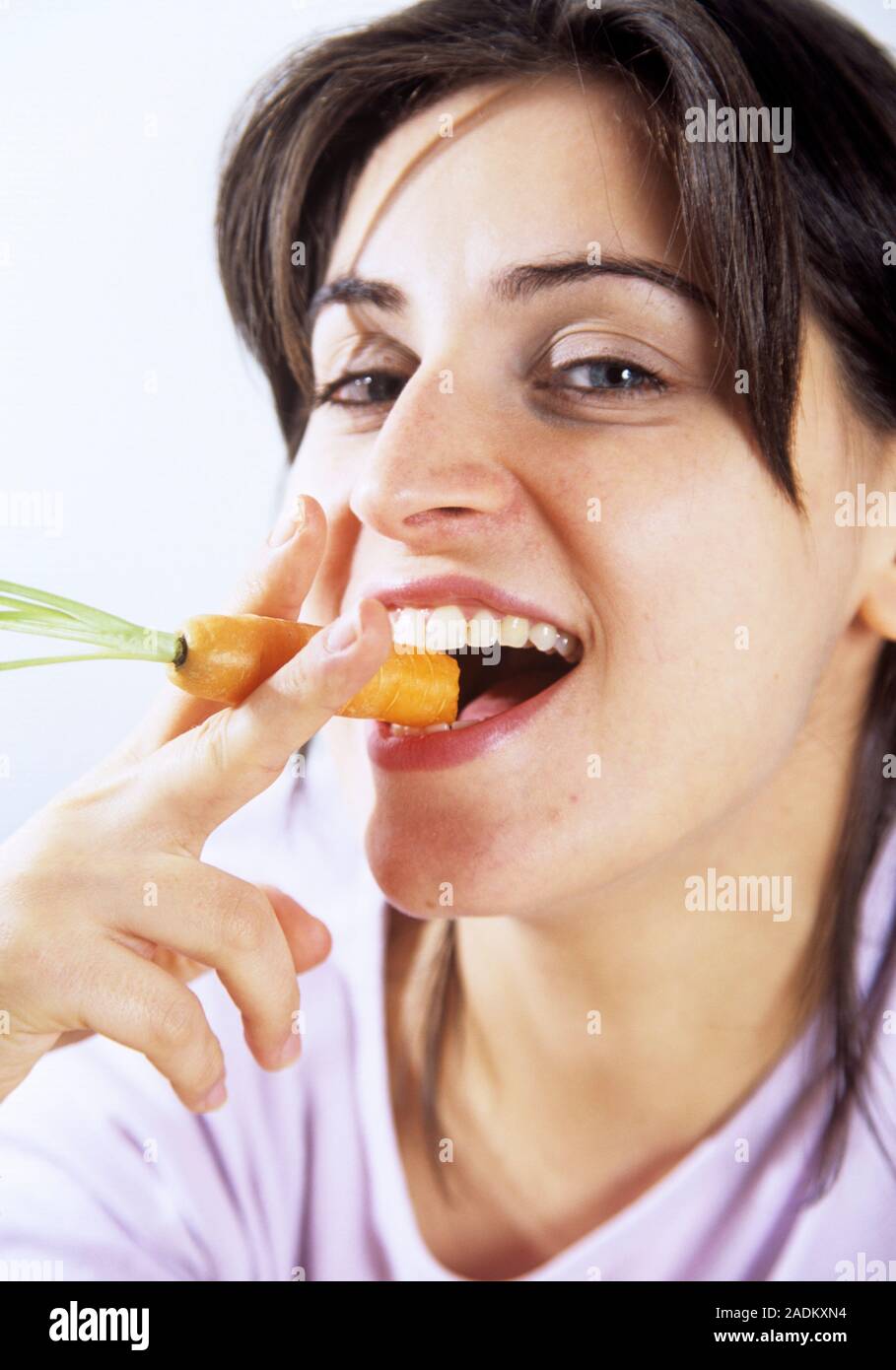 Healthy eating. Woman eating a carrot (Daucus carota). Carrots are rich ...