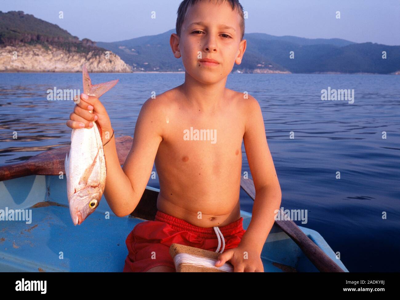 Child holding a fish. Young boy sitting in a rowing boat, proudly ...