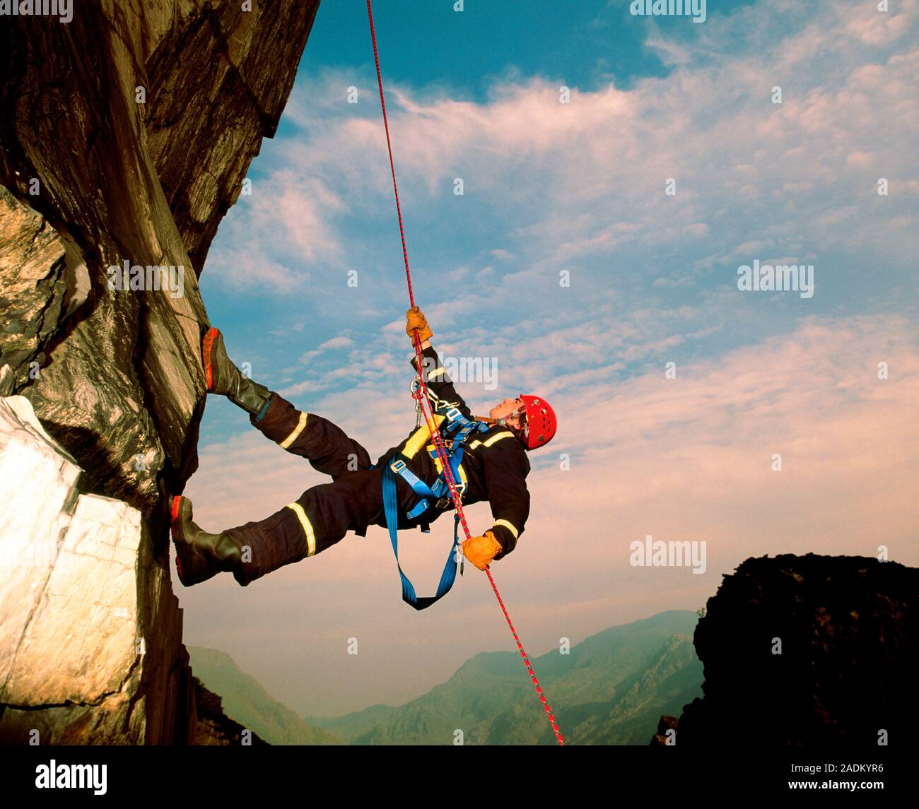 Rock climber descends a rocky cliff face by abseiling. The climber's ...