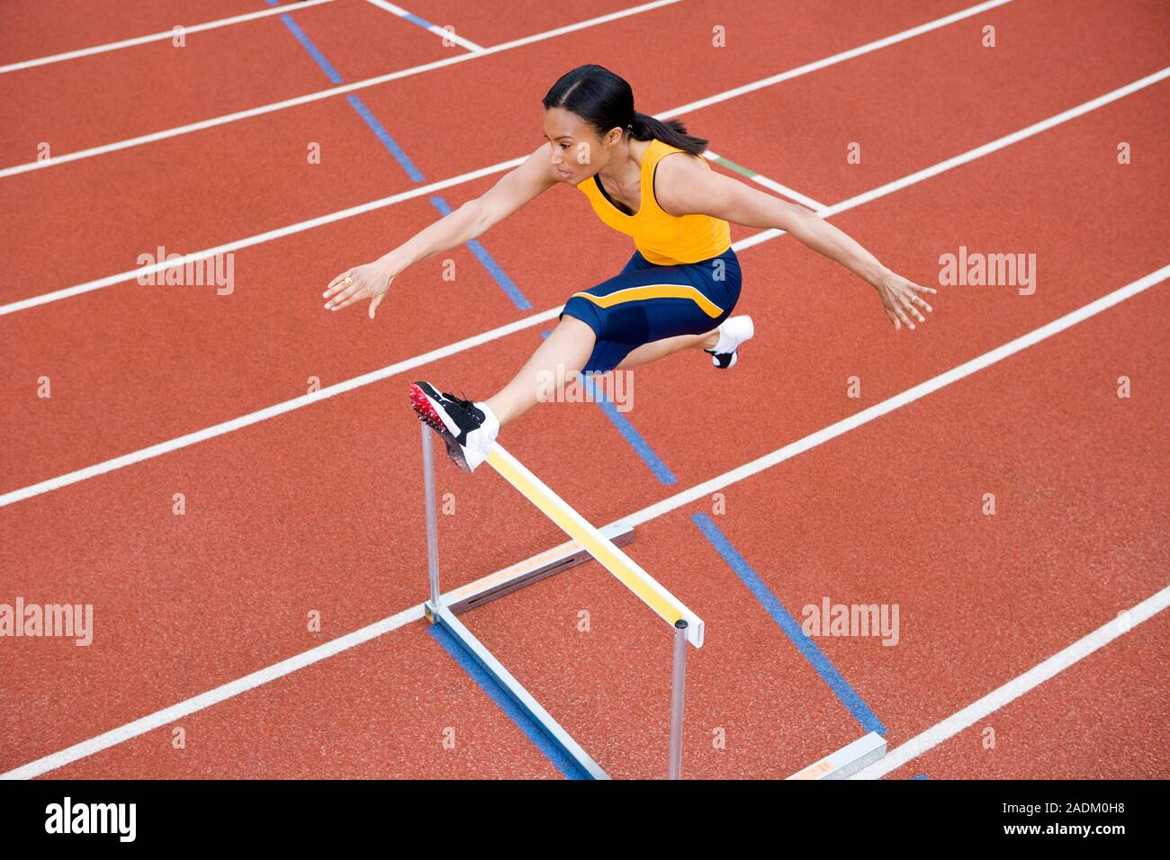 MODEL RELEASED. Athlete jumping over a hurdle on a race track. In ...