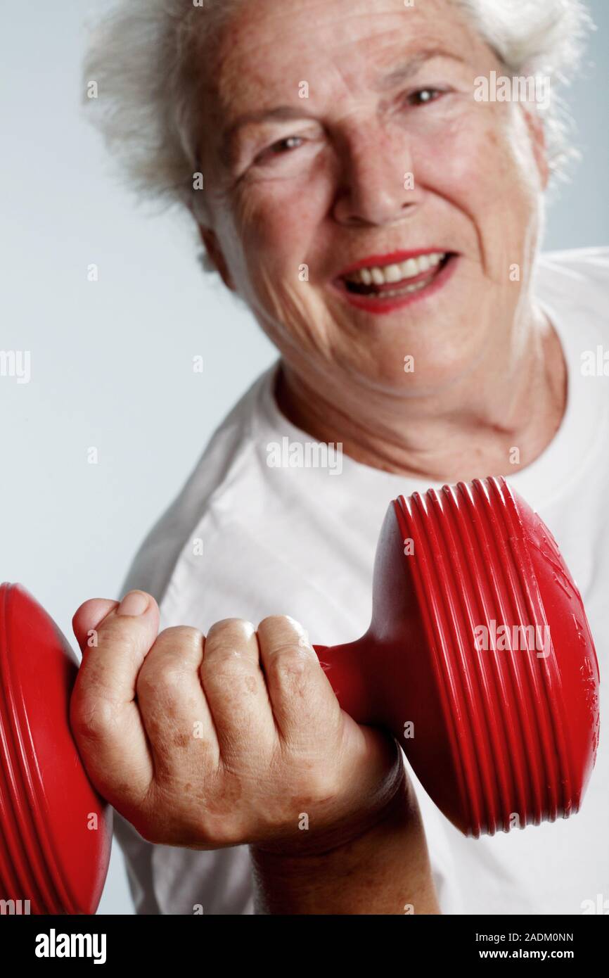 MODEL RELEASED. Elderly woman exercising her arm muscles by lifting a ...
