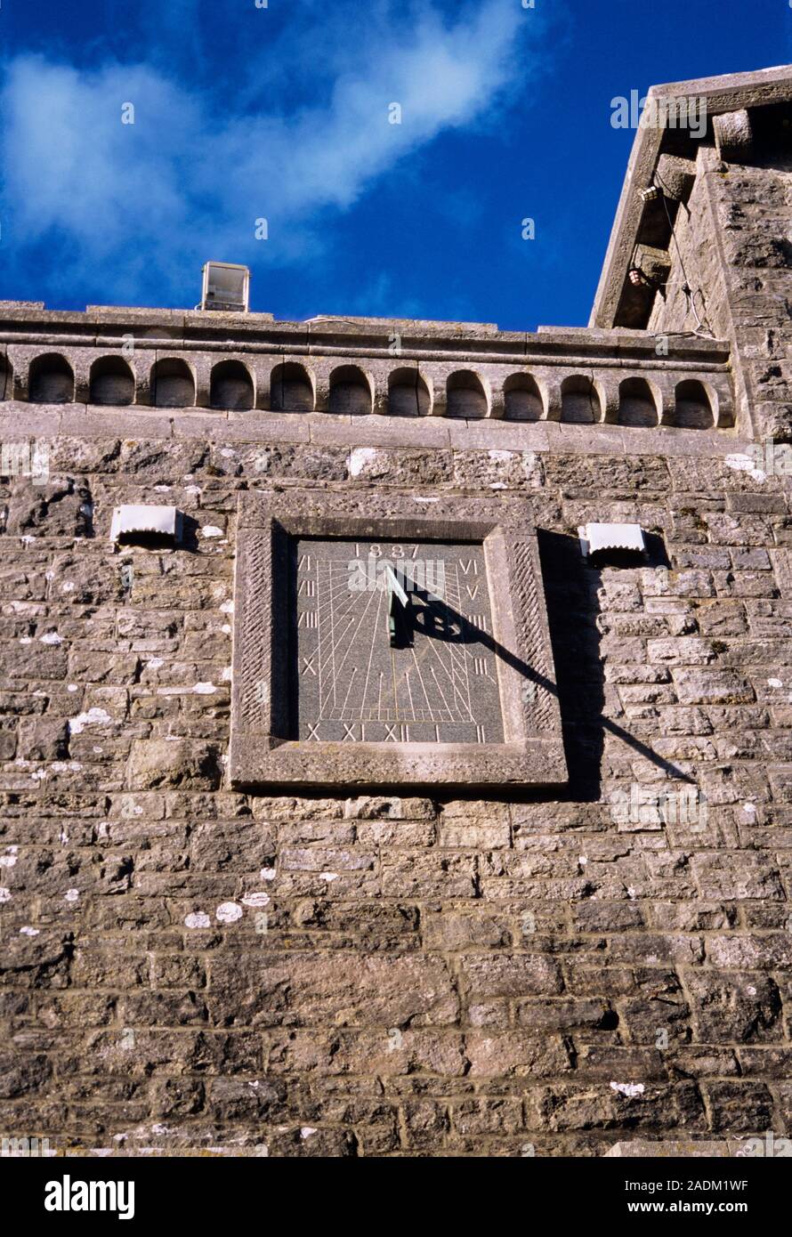 Sundial attached to the wall of a building. The sundial has a spike at ...