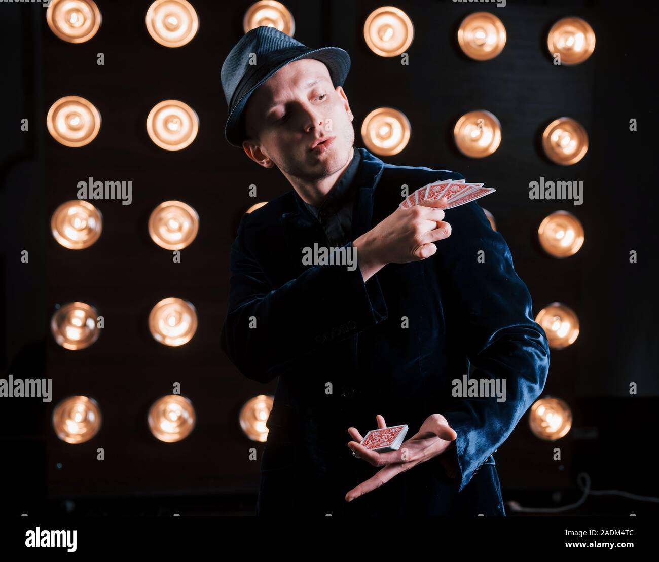 Showing professional tricks. Magician in black suit and with playing ...