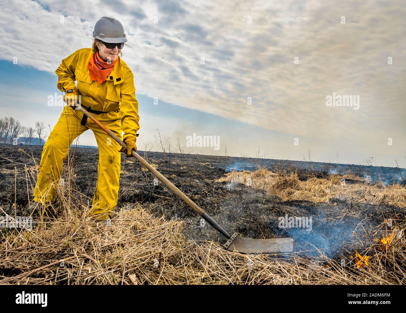 Female volunteer restoration worker uses a flapper to extinguish flames ...