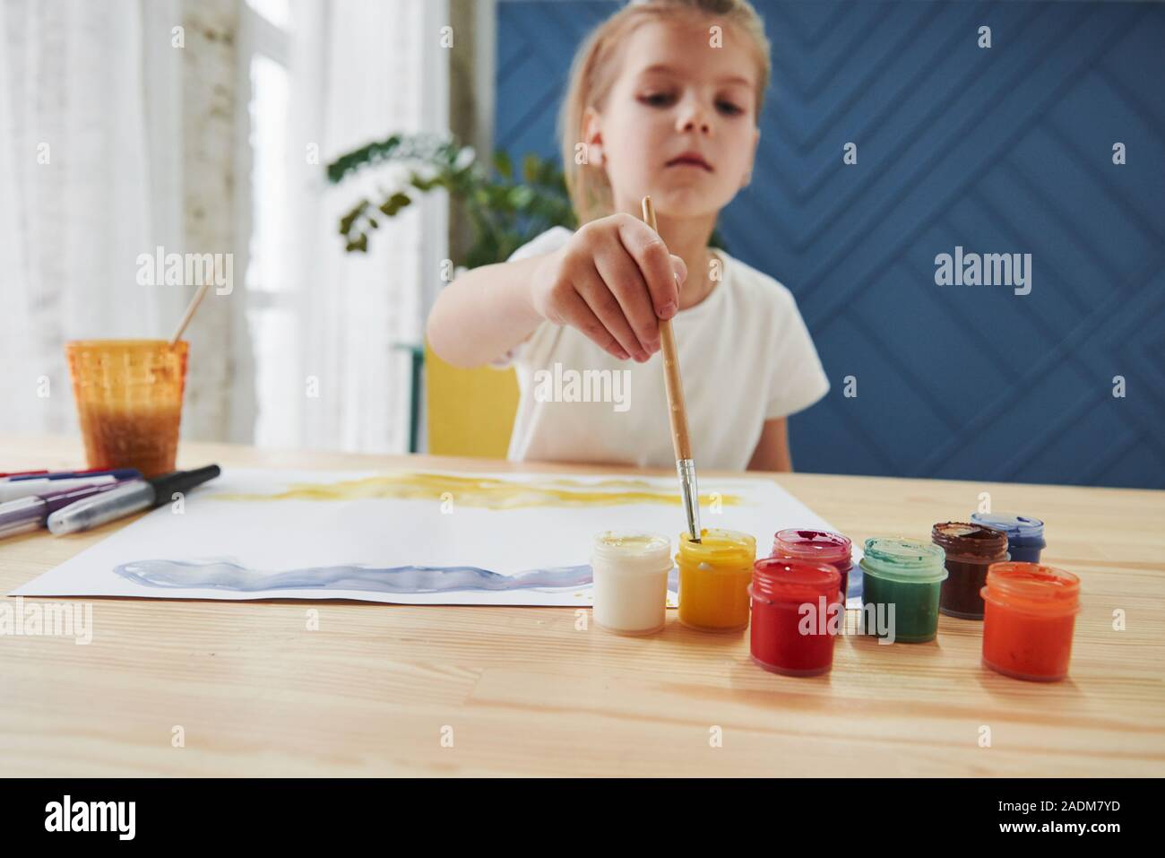 Takes the paint. Little girl is drawing by using gouache and brush ...