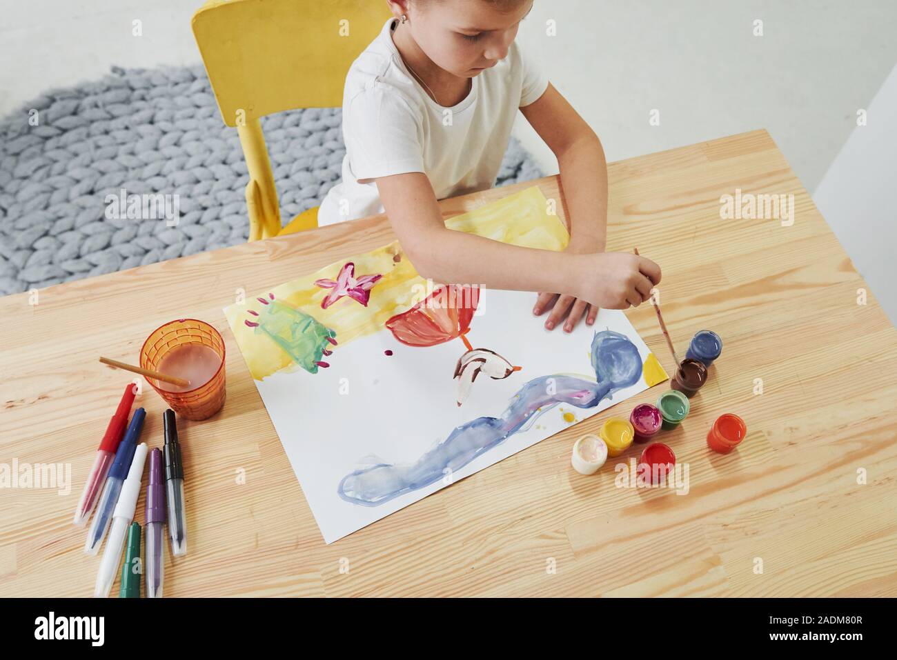 Picking brown color. Little girl is drawing by using gouache and brush ...