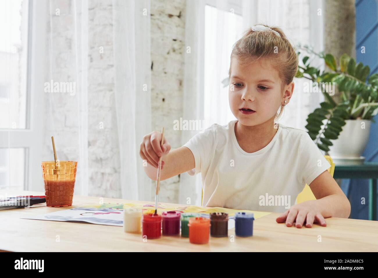 Busy child. Little girl is drawing by using gouache and brush. Learning ...