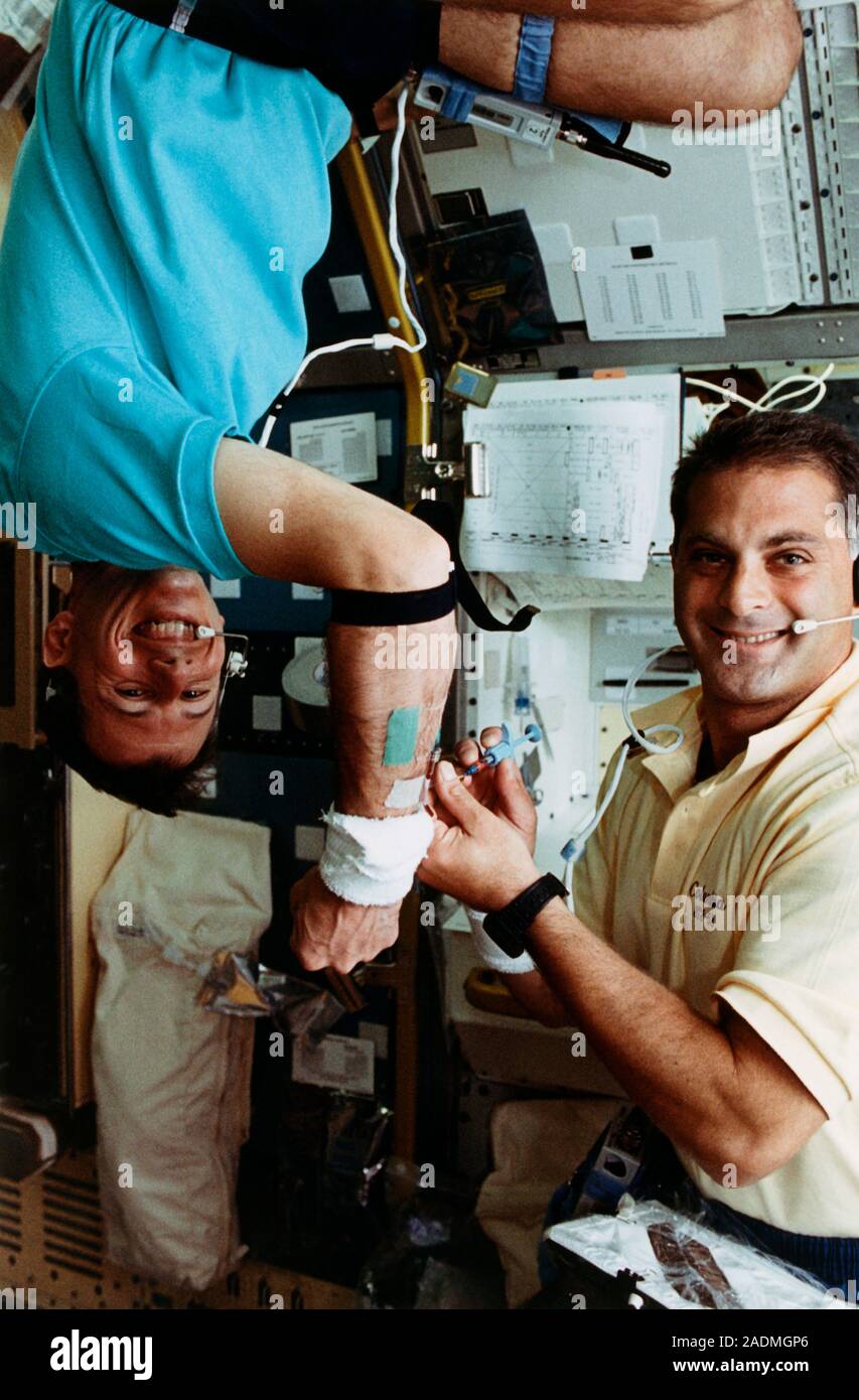 Spacelab experiment. Astronaut David Wolf (right) taking a blood sample ...
