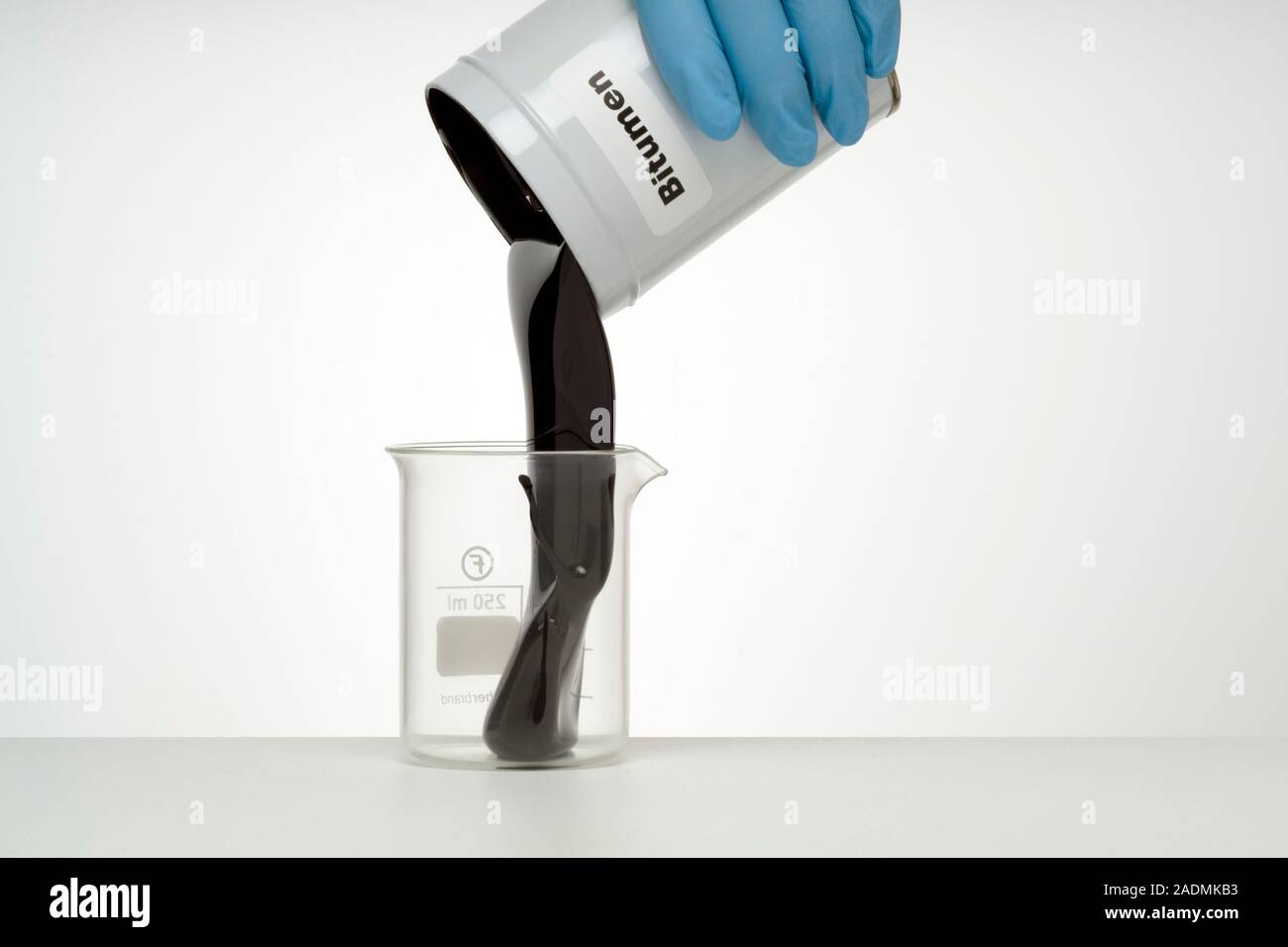 Bitumen being poured into a beaker. Bitumen is a product of the ...