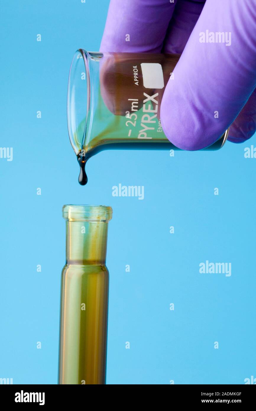 Crude oil being poured from a glass beaker into the neck of a glass ...