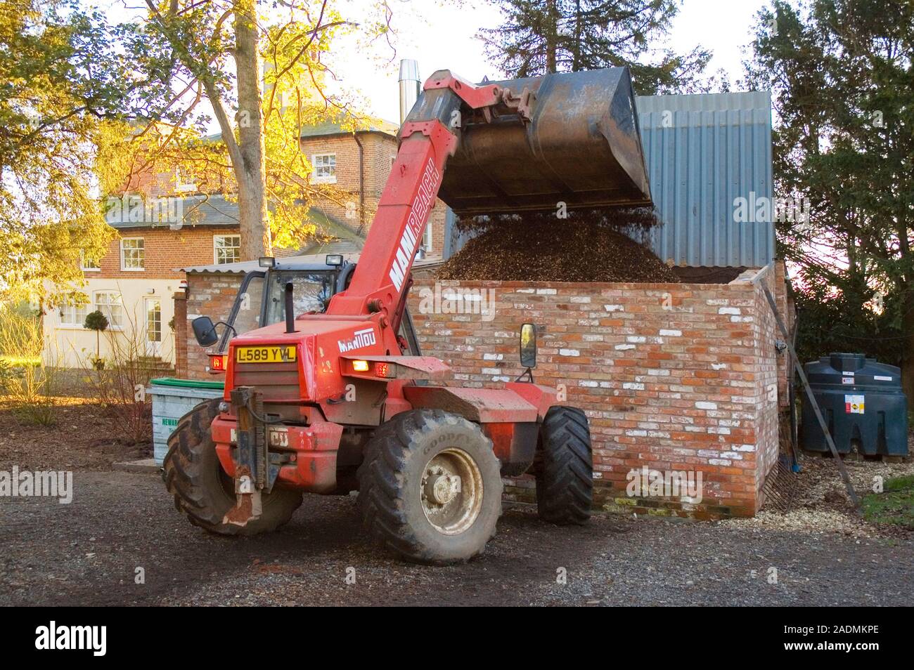 MODEL RELEASED. Tractor loading wood chips into a brick storage space ...