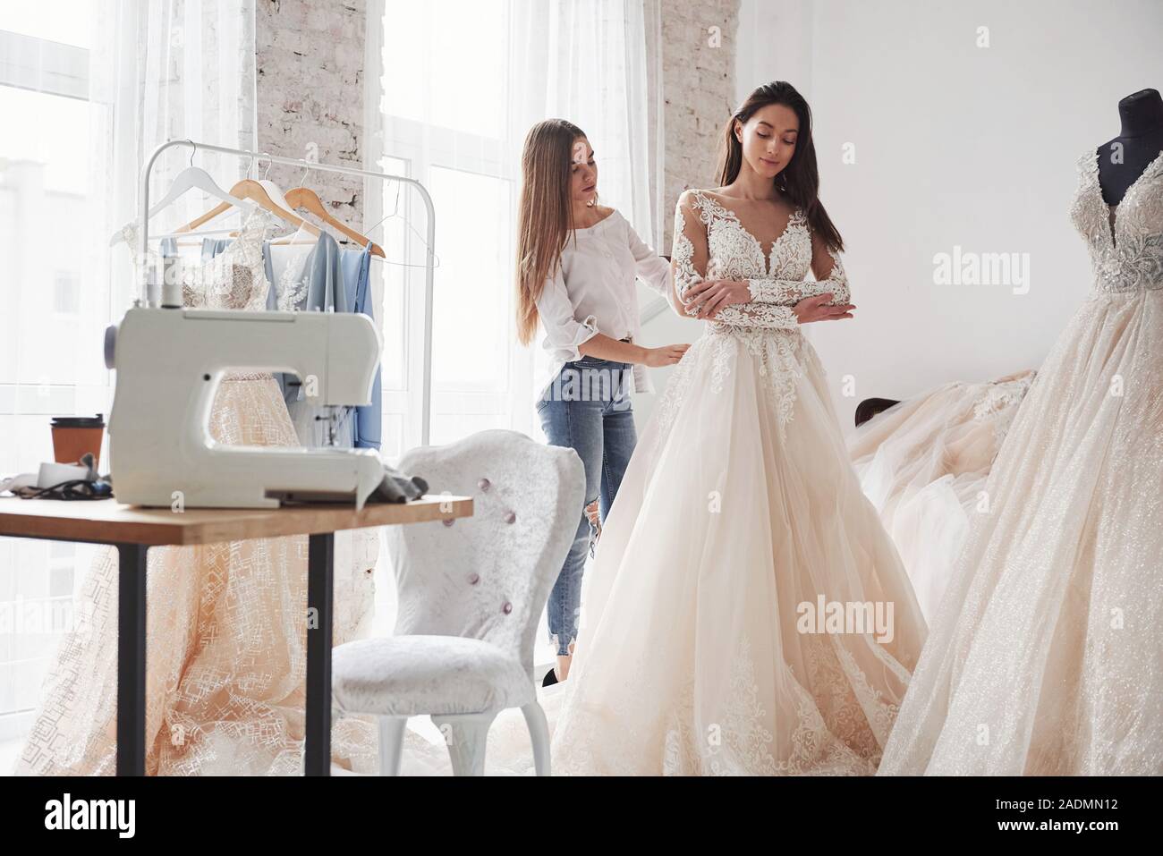 Girl is helping bride. The process of fitting the dress in the studio ...