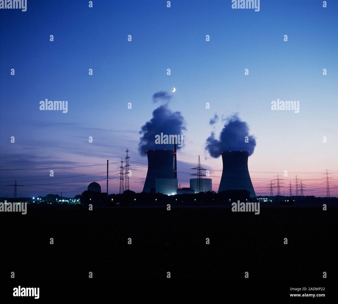 Nuclear power station at dusk, with cooling towers venting water vapour ...
