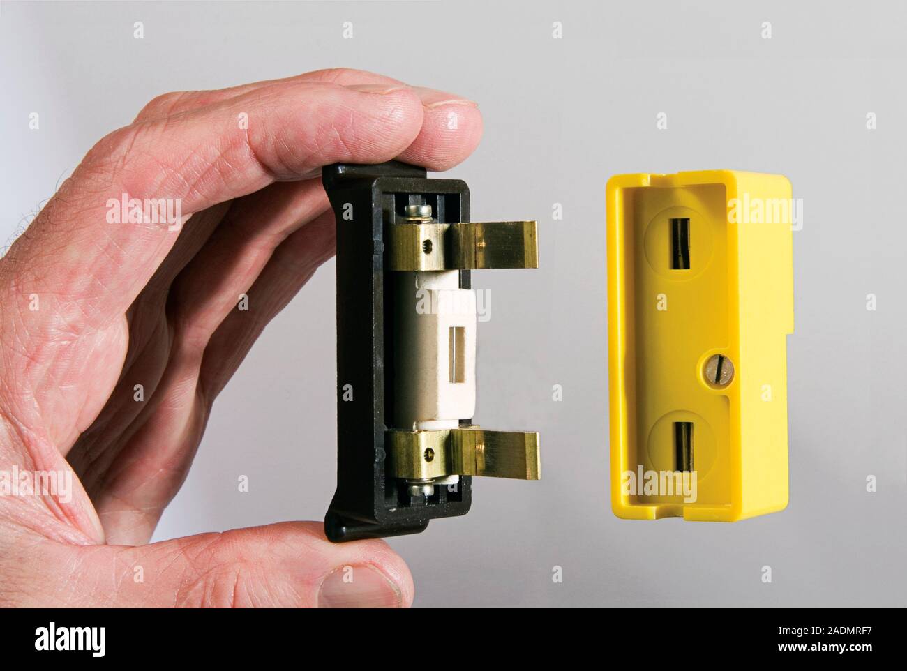 Fuse. Hand inserting a fuse into its socket. The yellow colour of the ...