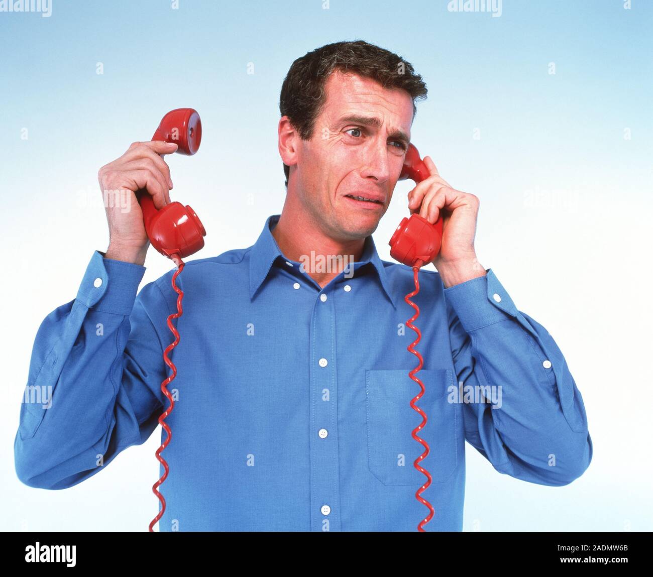 Communication stress. Stressed man holding two telephone receivers ...