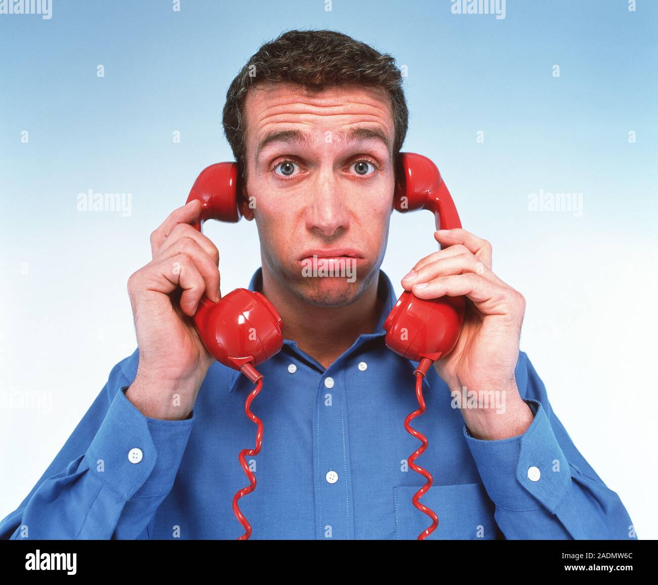 Communication stress. Stressed man holding two telephone receivers ...