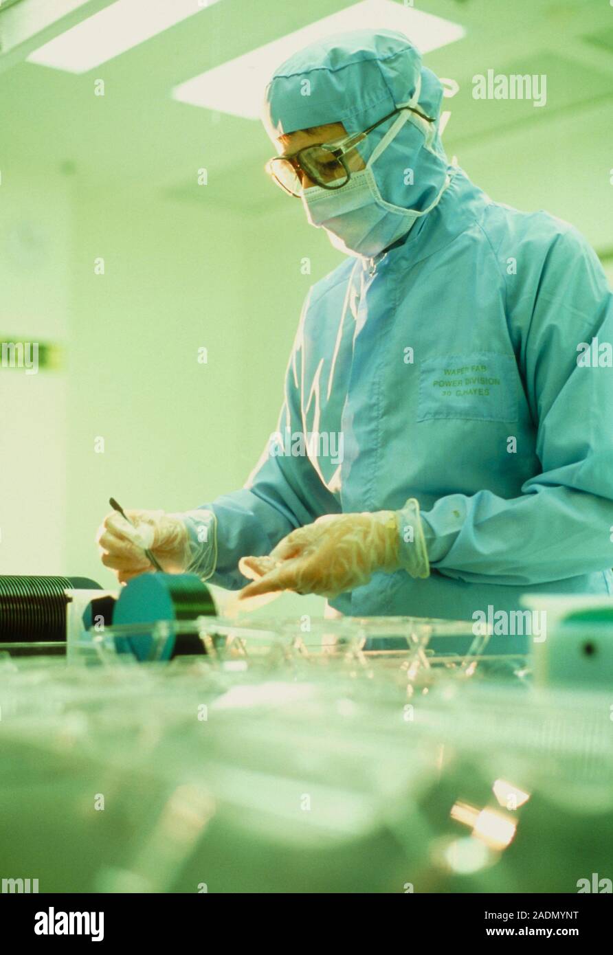 Microchip manufacture. Technician in a clean room arranges ...