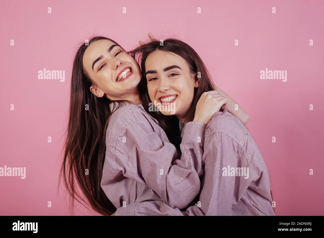 Sincere emotions. Two sisters twins standing and posing in the studio ...