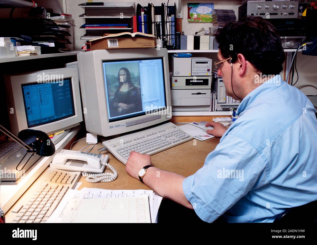 Office computing. A businessman, sitting at his desk, uses a computer ...