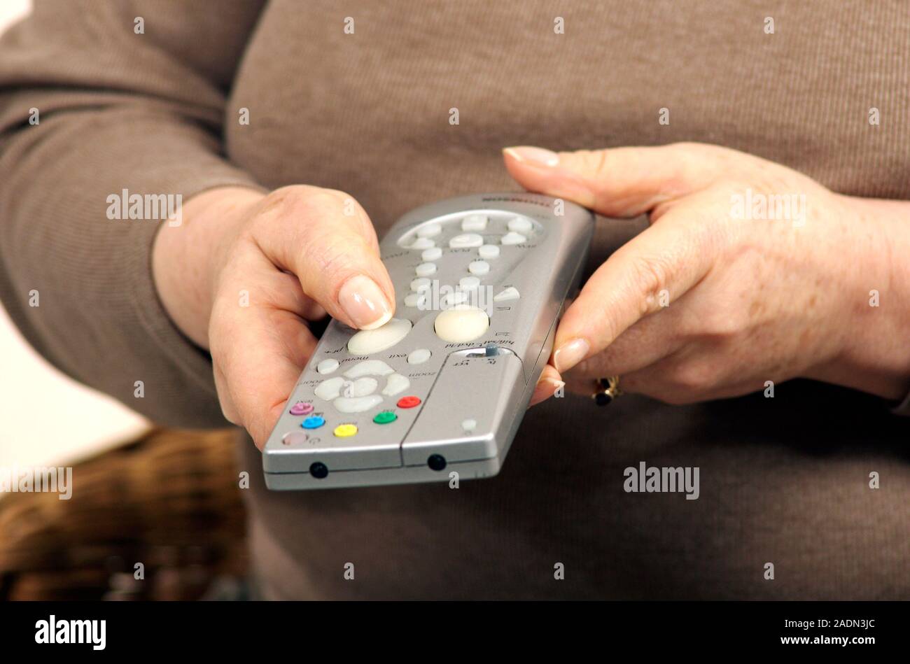 MODEL RELEASED. Remote control use. Woman pressing a button on a remote ...