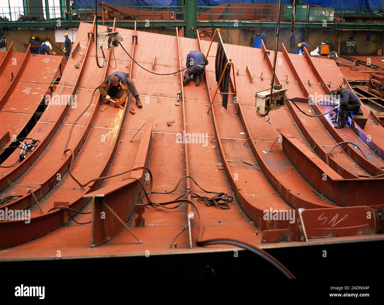 Shipbuilding. Workers welding the prefabricated segments of a ship's hull in a dry dock in ...