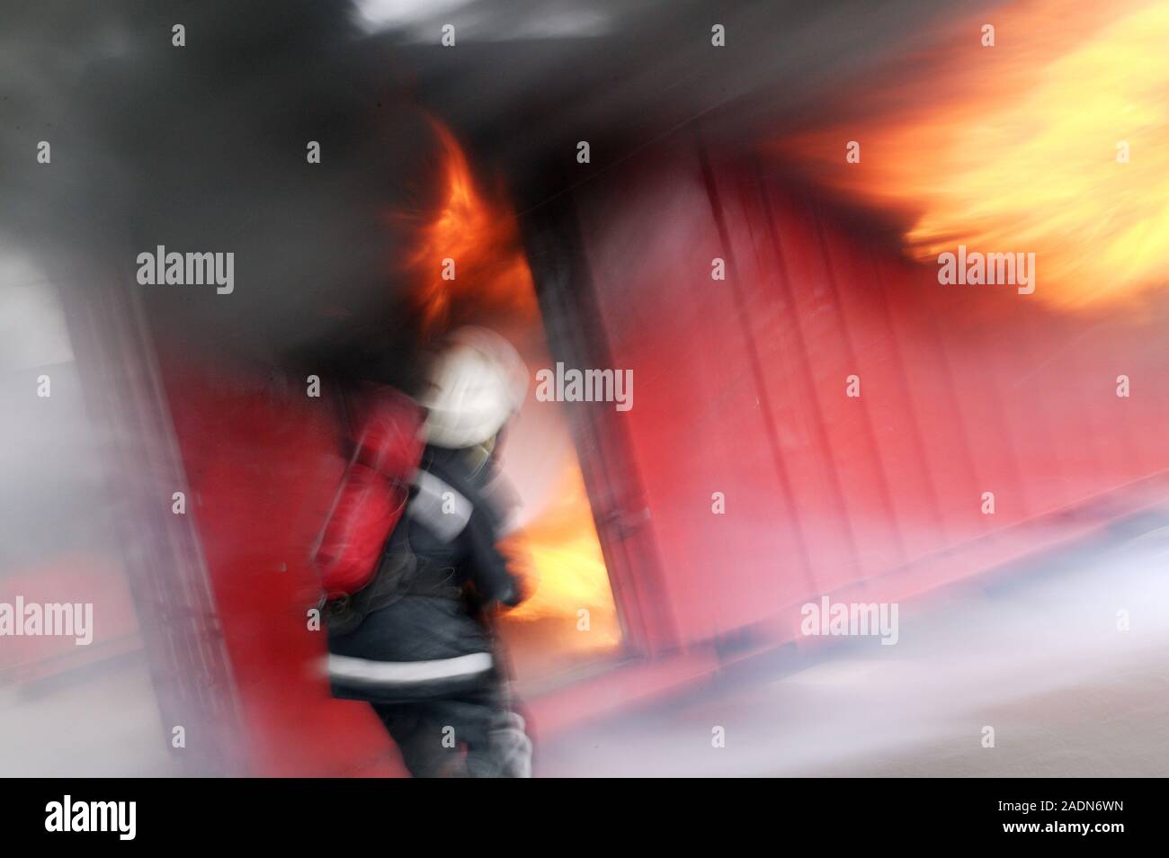 Firefighter running towards a burning building. The firefighter is ...