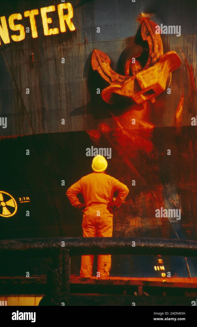 Rusting ship anchor. Worker contemplates a rusting ship anchor. Rust is ...