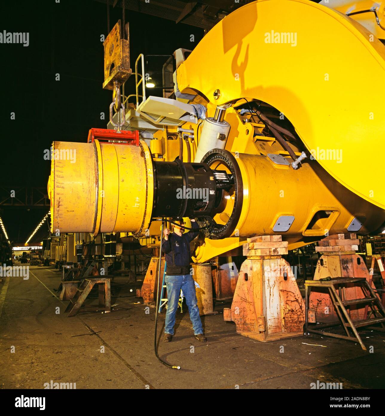 Wheel axle. Worker positioning a wheel axle on a wheel loader vehicle ...