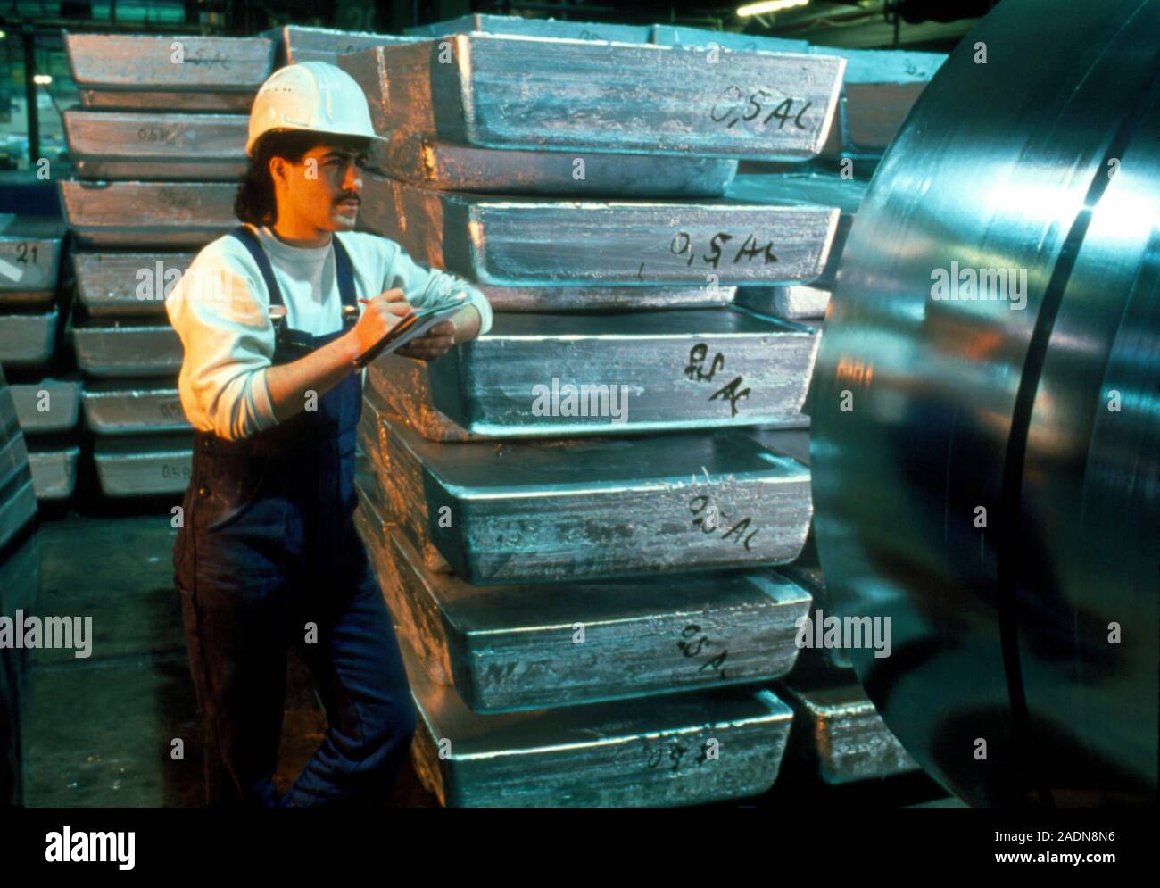 POSED BY MODEL. Zinc production. Technician making notes beside bars of ...
