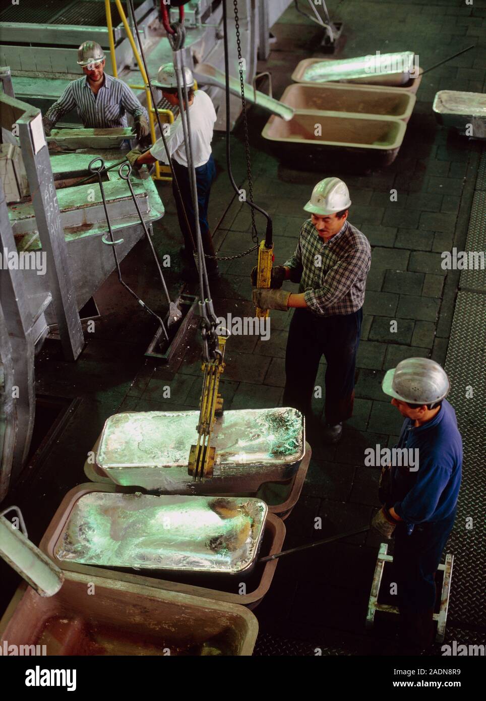 MODEL RELEASED. Aluminium processing plant. Worker removing bars of ...
